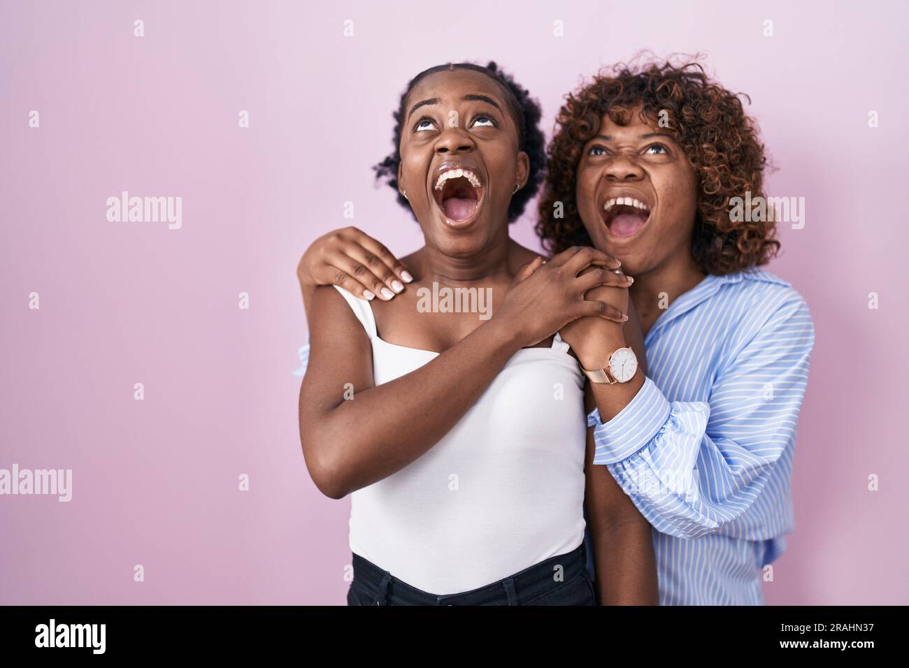Two african women standing over pink background angry and mad screaming ...