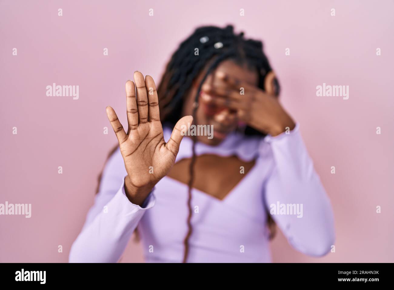 African woman with braided hair standing over pink background covering ...
