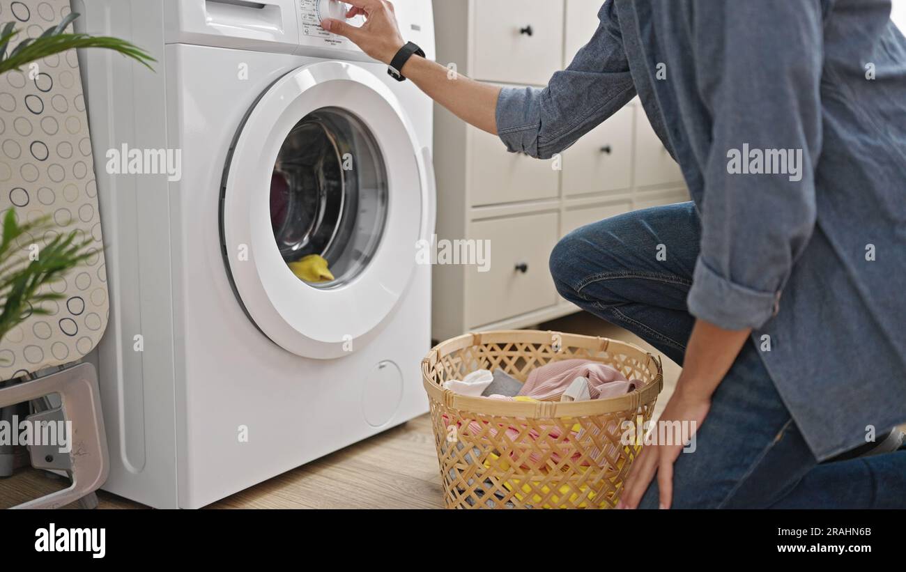 Young hispanic man washing clothes starting washing machine at laundry ...