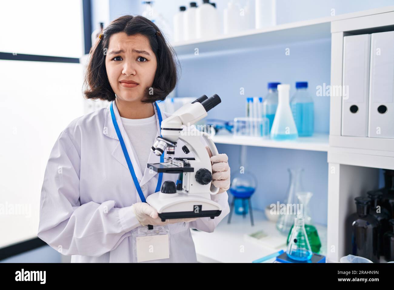 Young hispanic woman working at scientist laboratory holding microscope ...