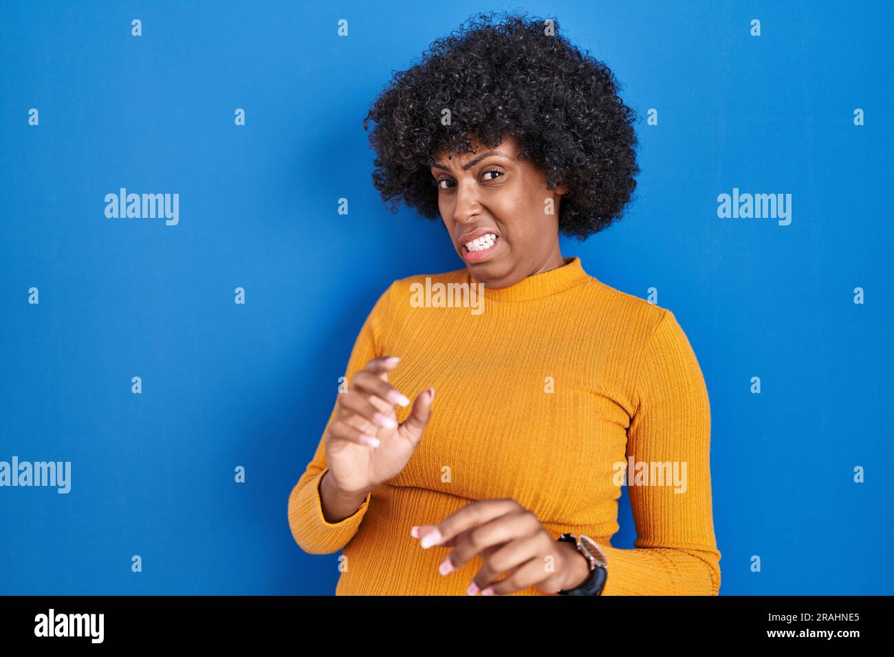 Black woman with curly hair standing over blue background disgusted ...