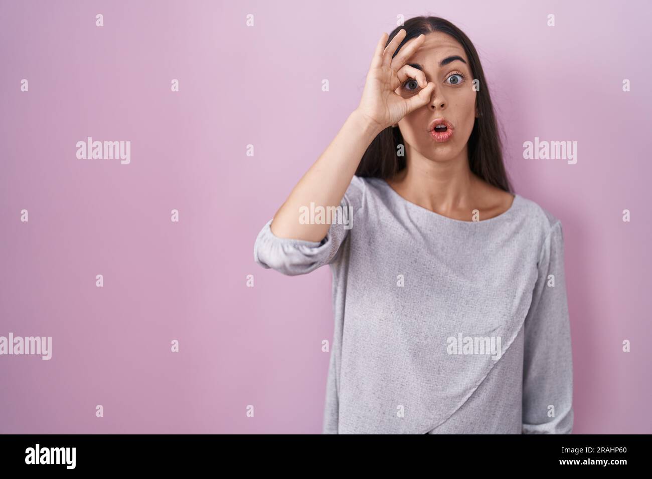Young brunette woman standing over pink background doing ok gesture ...