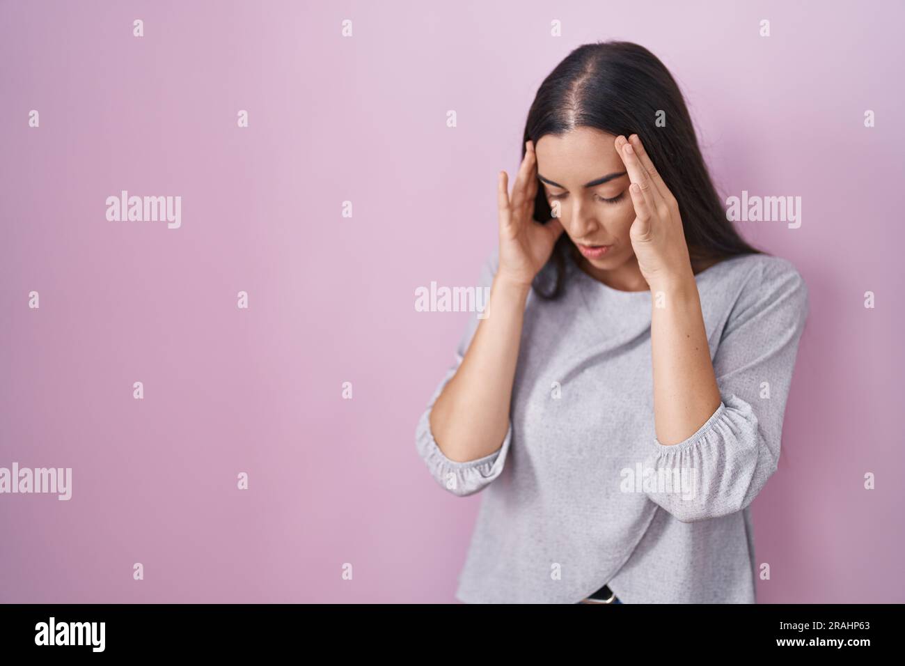 Young brunette woman standing over pink background with sad expression ...