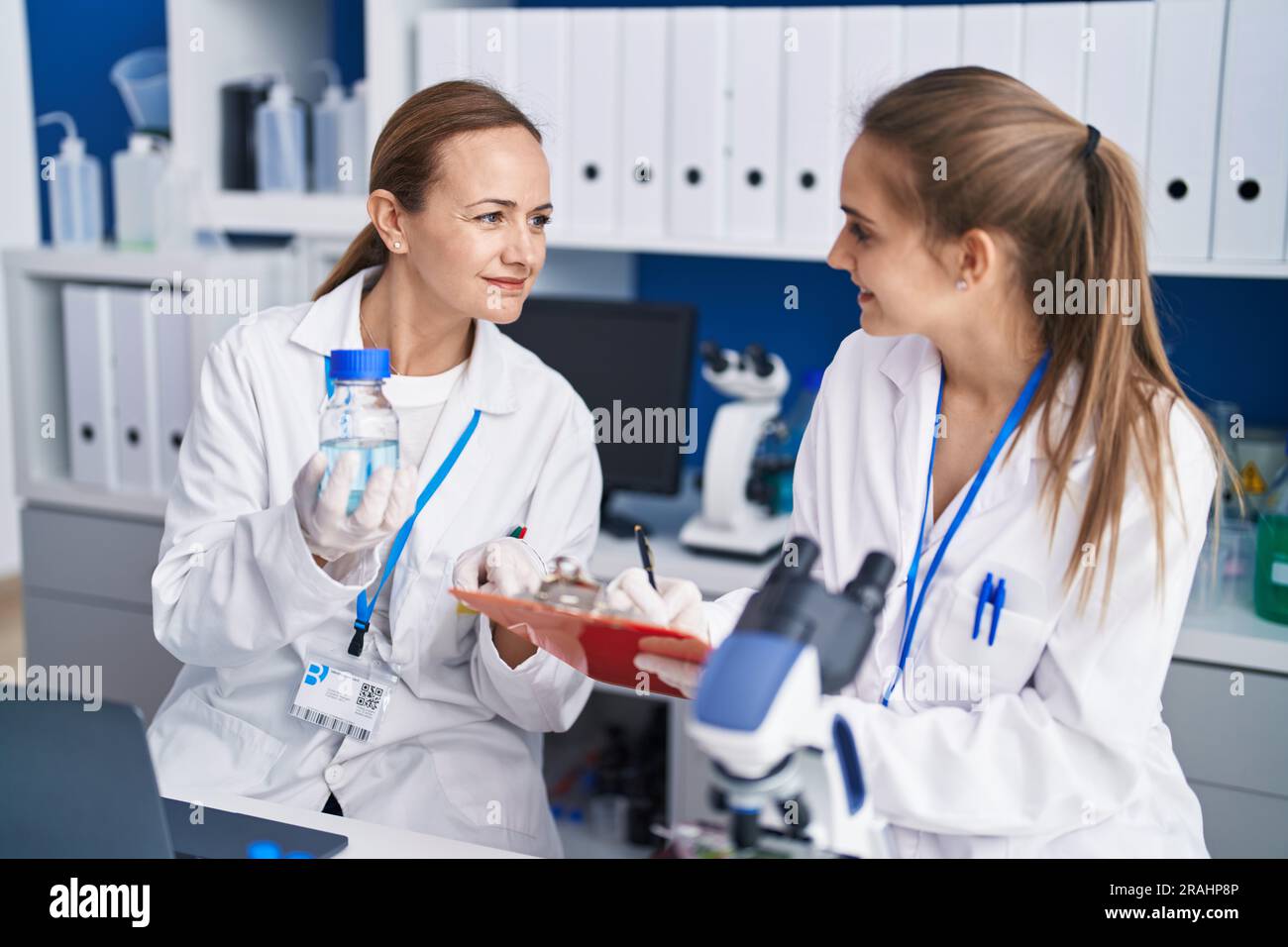 Two women scientists write on document measuring liquid at laboratory ...