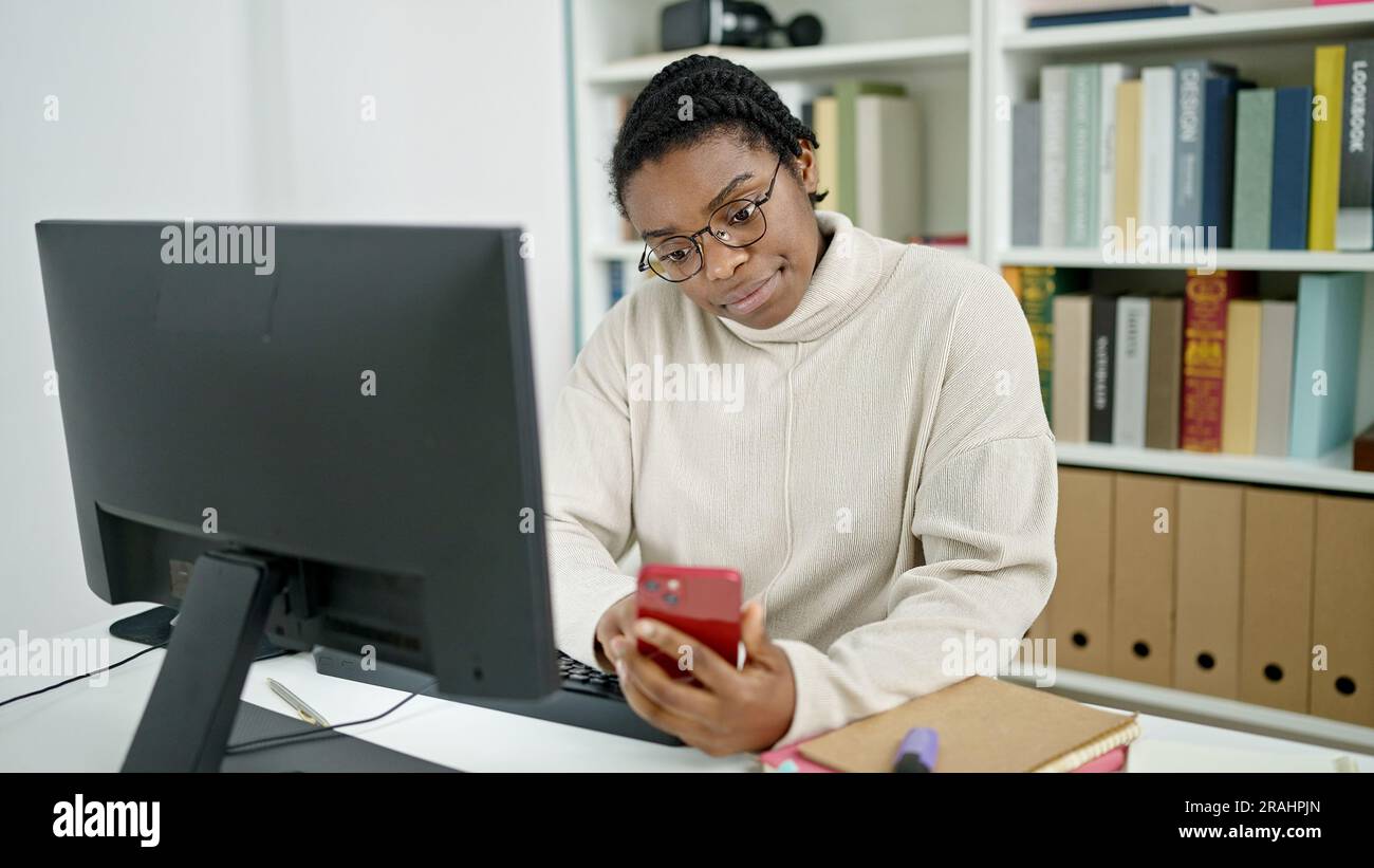 African american woman student using computer and smartphone at library ...