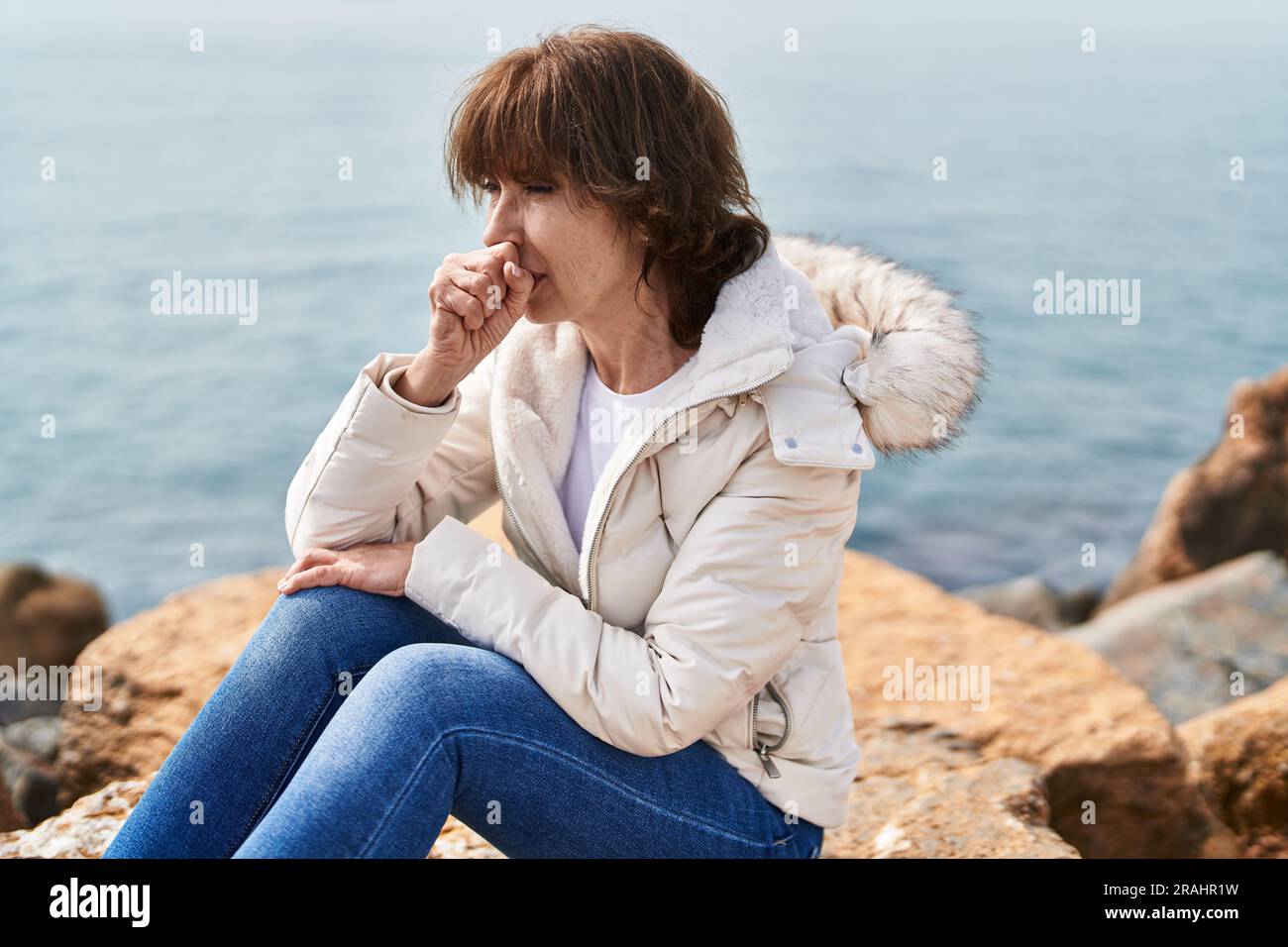 Middle age woman coughing sitting on the rock at seaside Stock Photo ...