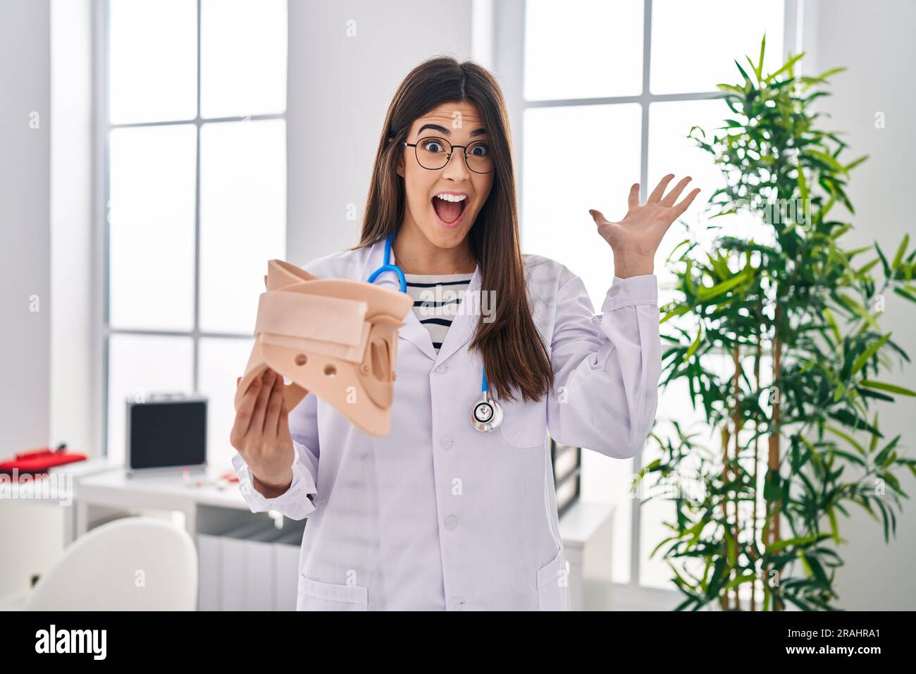 Young brunette doctor woman holding cervical neck collar celebrating ...