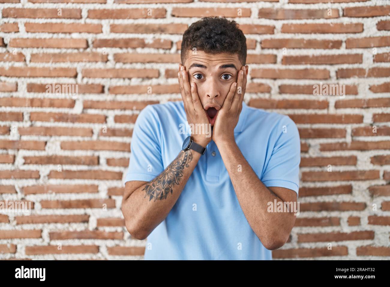 Brazilian young man standing over brick wall afraid and shocked ...