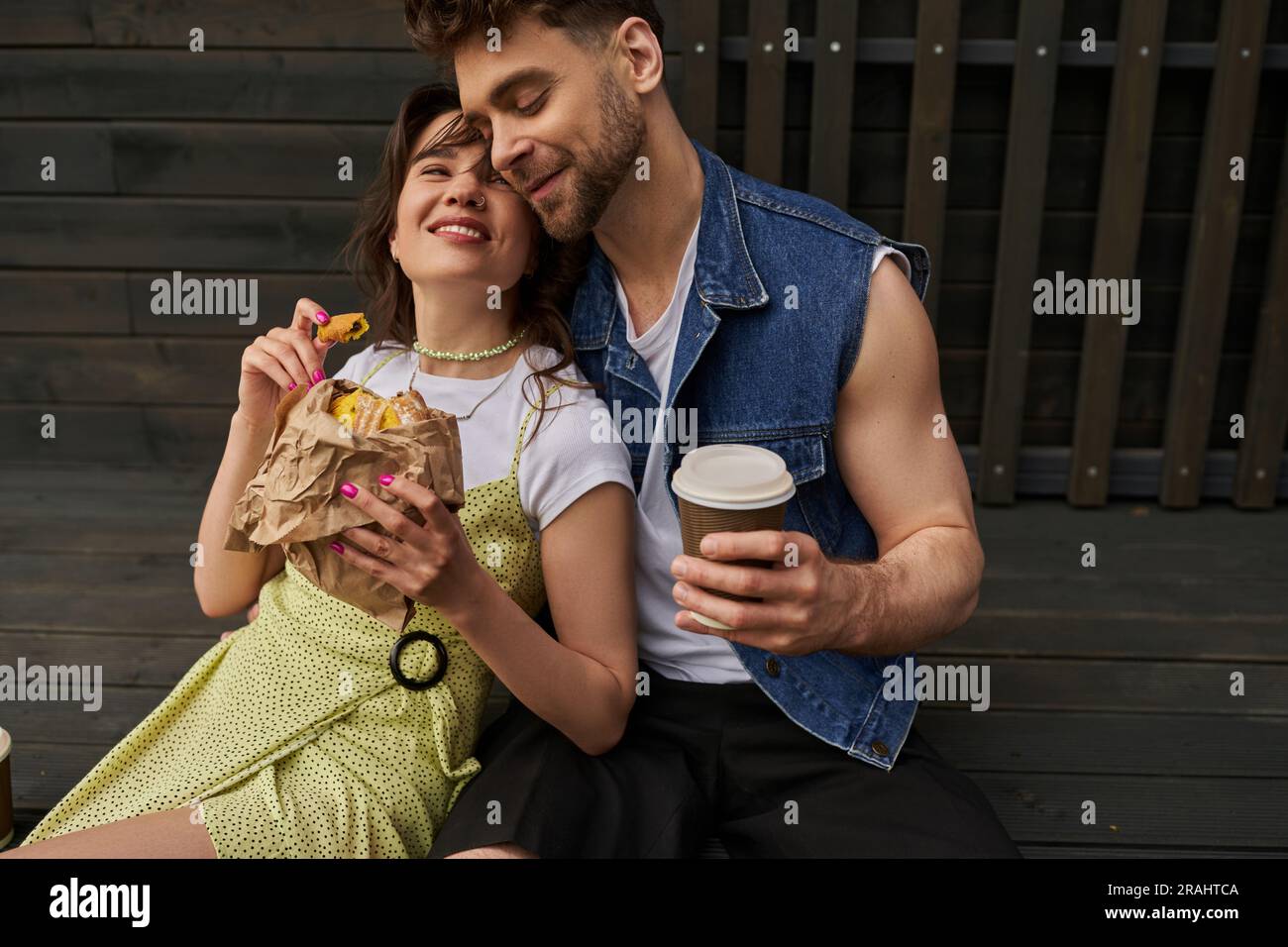 Joyful and stylish woman in sundress holding fresh bun and sitting near ...