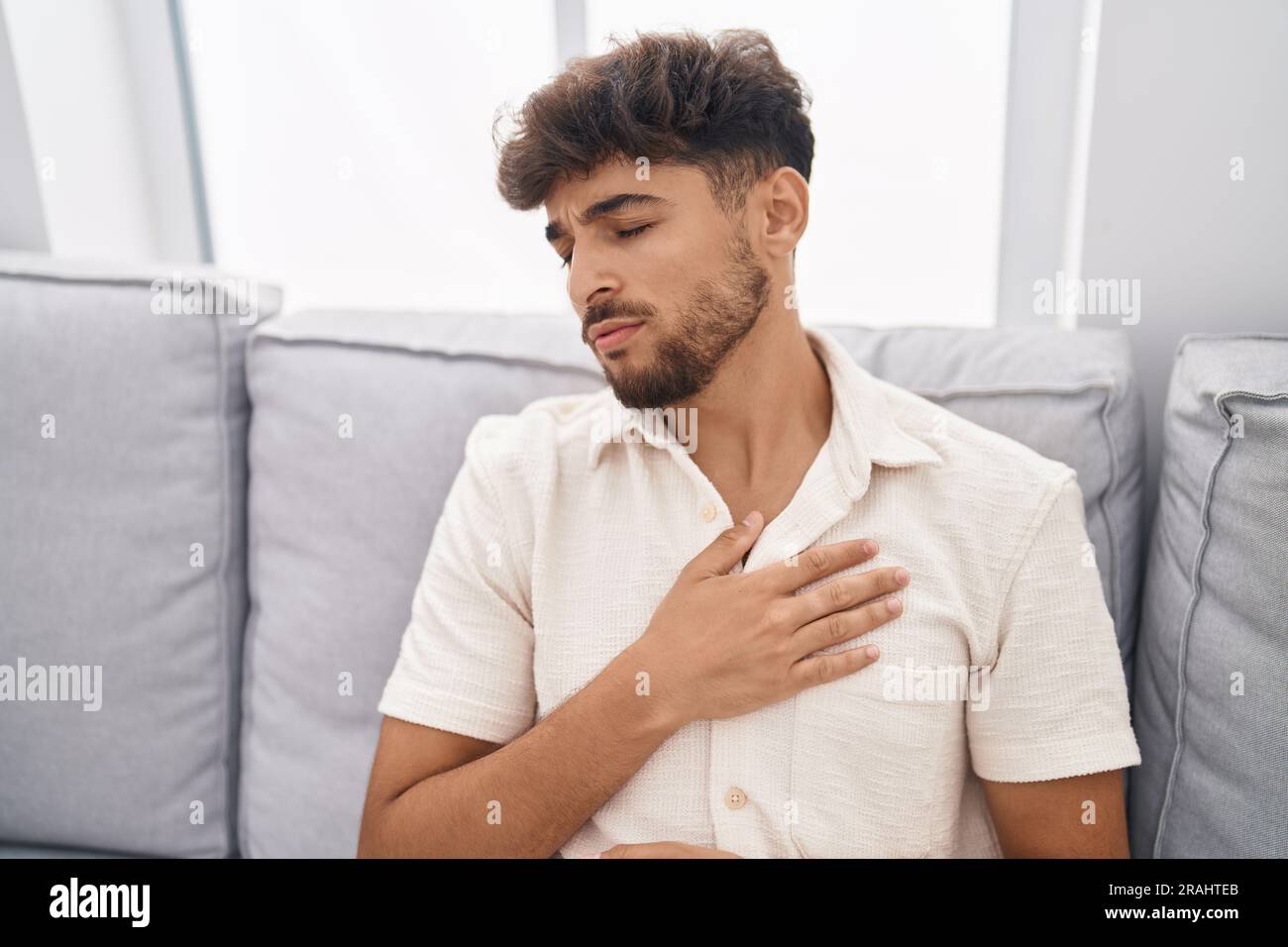 Young arab man suffering heart attack sitting on sofa at home Stock ...