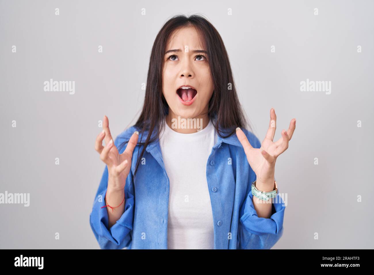 Young chinese woman standing over white background crazy and mad ...