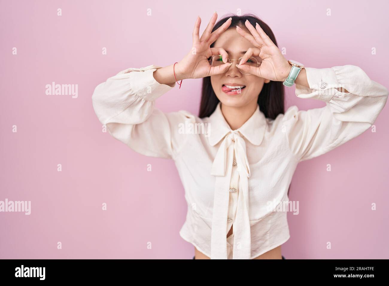 Young chinese woman standing over pink background doing ok gesture like ...
