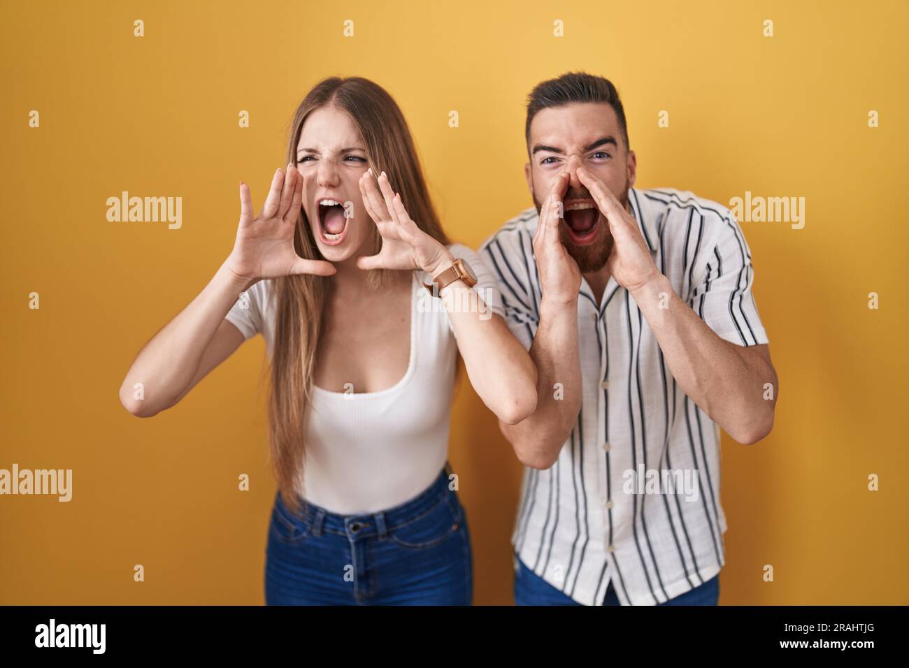 Young couple standing over yellow background shouting angry out loud ...