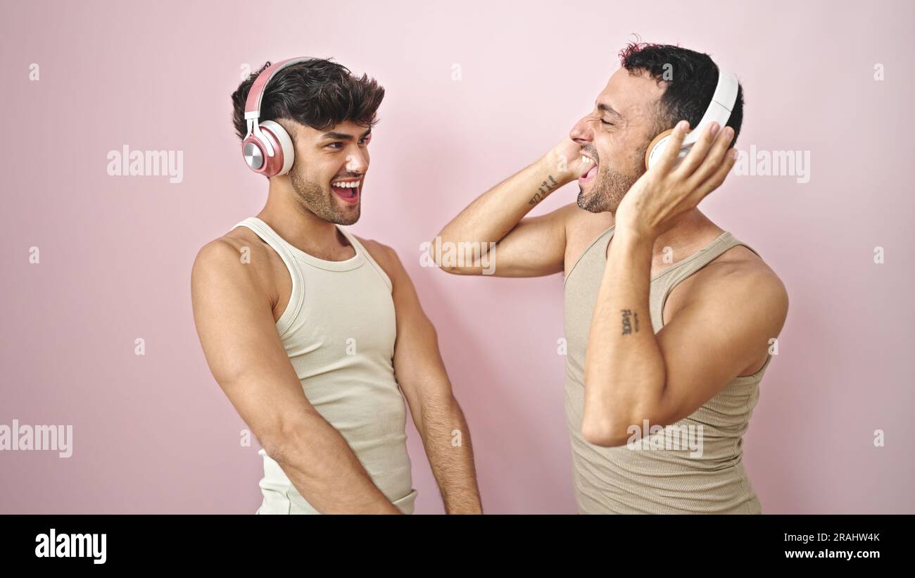 Two men couple listening to music dancing together over isolated pink ...