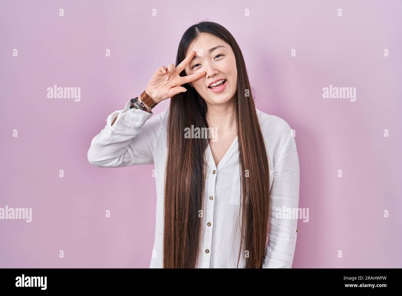 Chinese young woman standing over pink background doing peace symbol ...