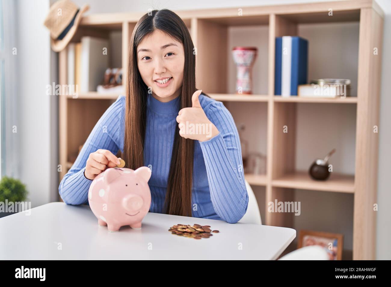 Chinese young woman putting coin in piggy bank smiling happy and ...