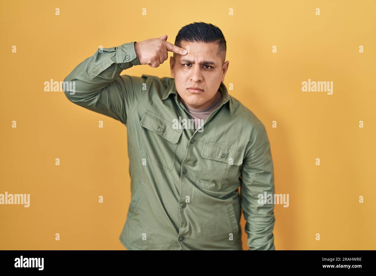 Hispanic young man standing over yellow background pointing unhappy to ...