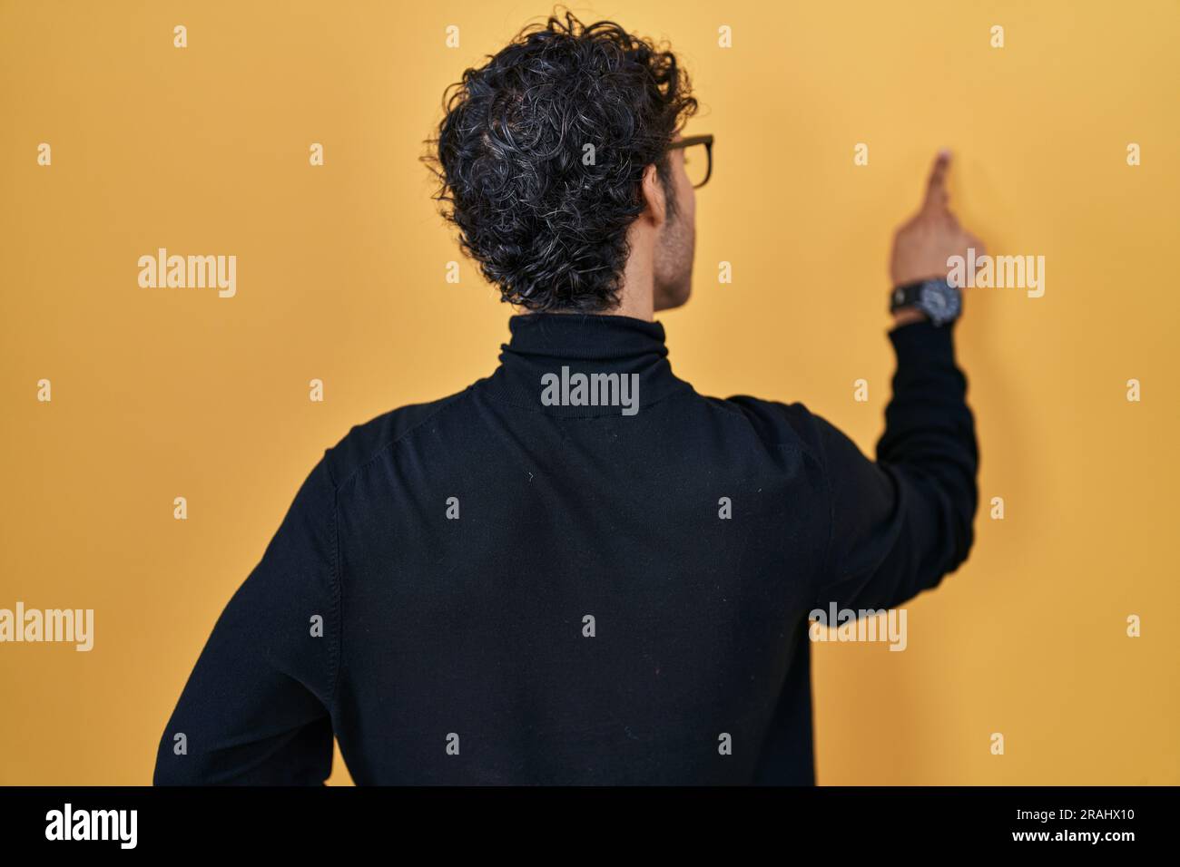 Hispanic man standing over yellow background posing backwards pointing ...