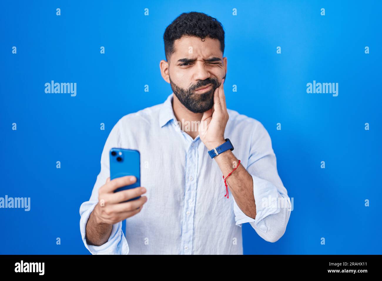 Hispanic Man With Beard Using Smartphone Typing Message Touching Mouth