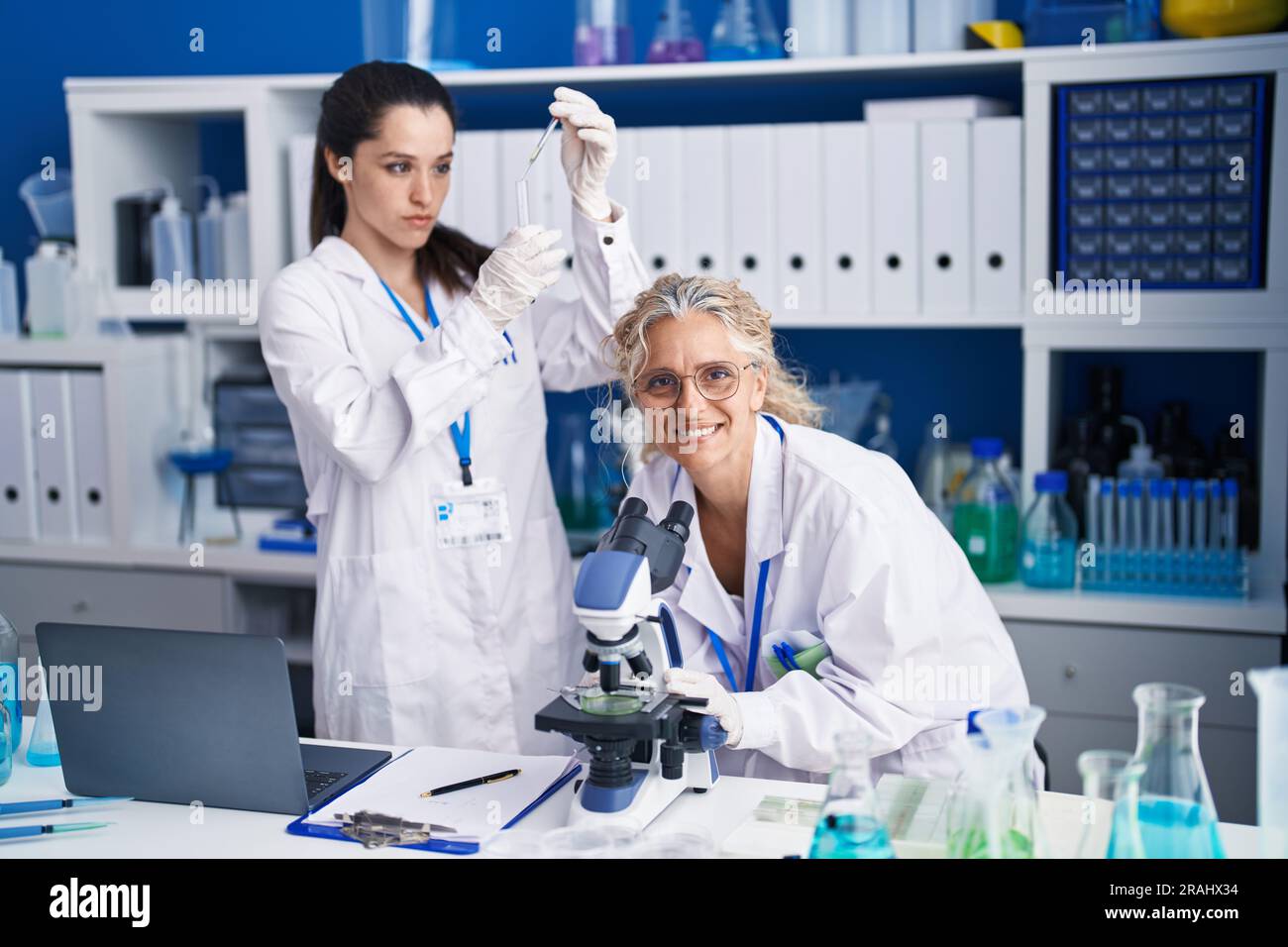Two women scientists using microscope measuring liquid at laboratory ...