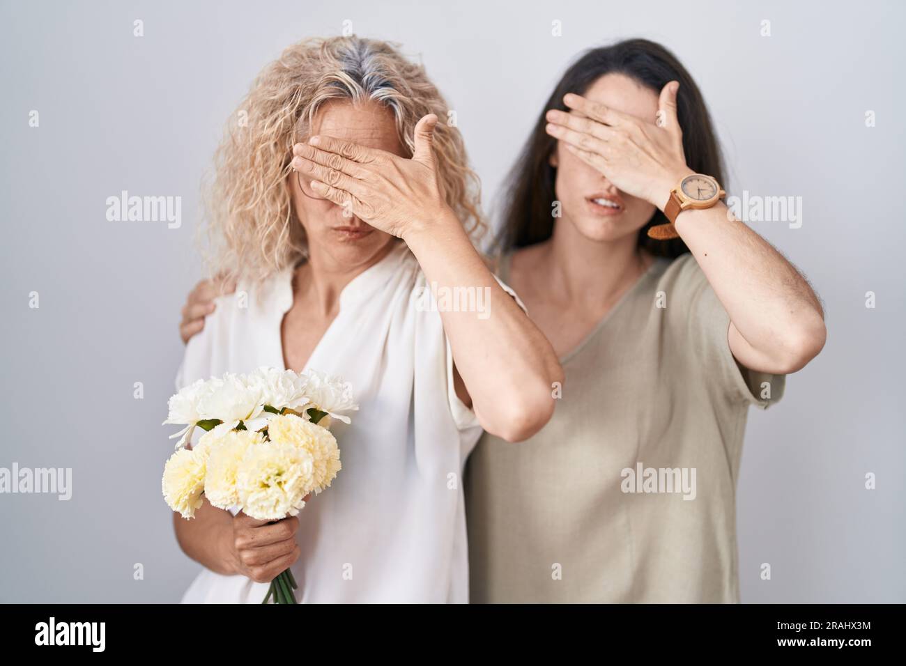 Mother and daughter holding bouquet of white flowers covering eyes with ...