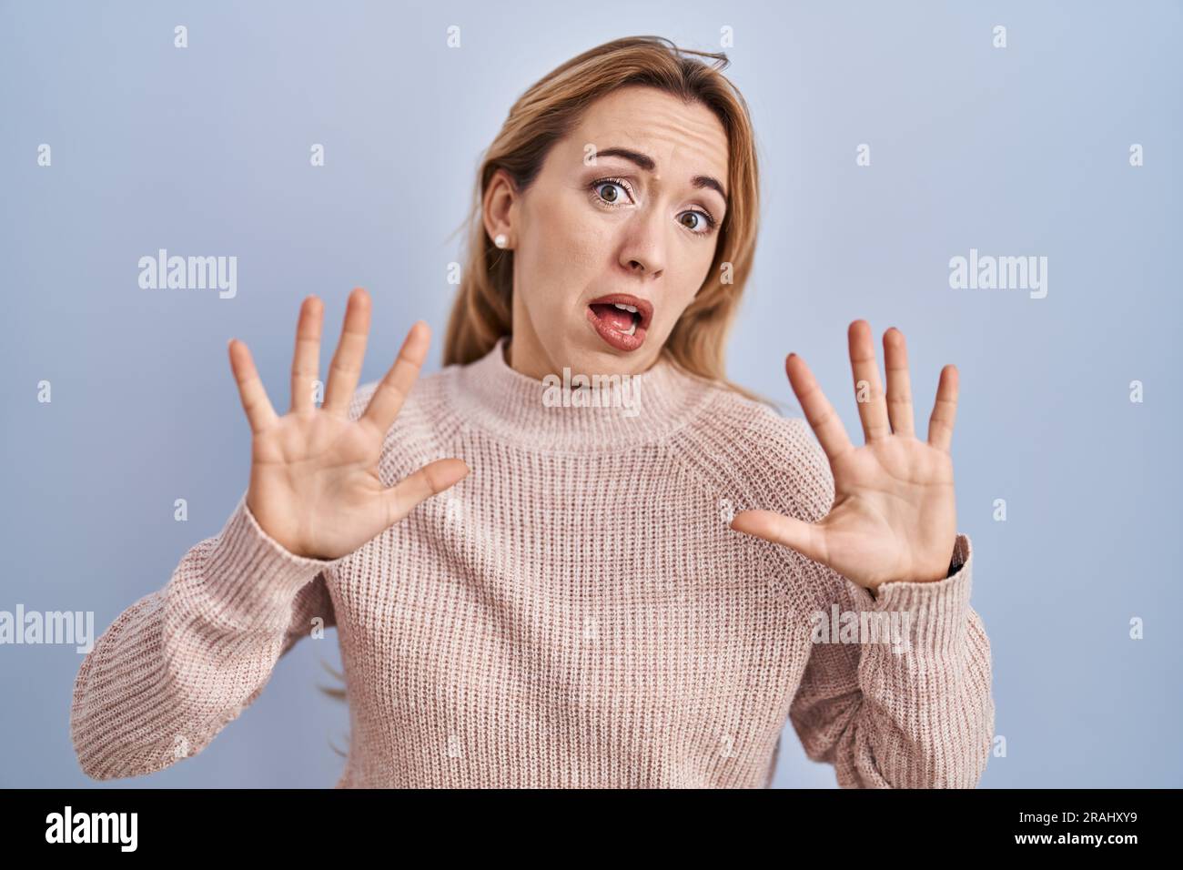 Hispanic woman standing over blue background afraid and terrified with ...