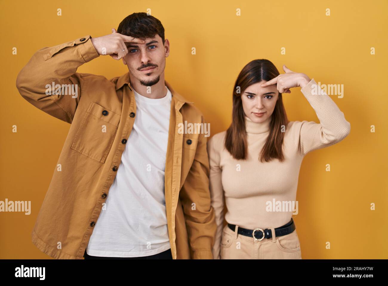Young hispanic couple standing over yellow background pointing unhappy ...