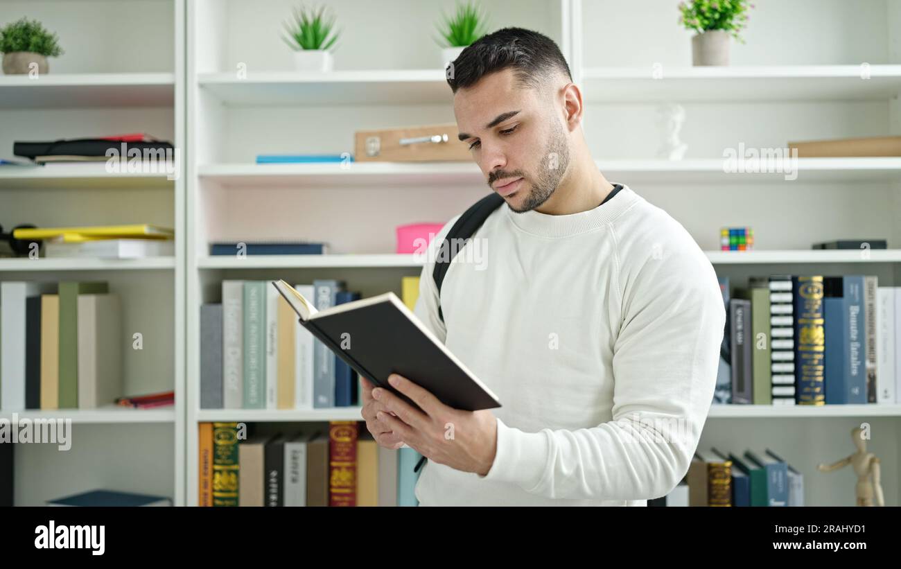 Young hispanic man standing reading book at library university Stock ...