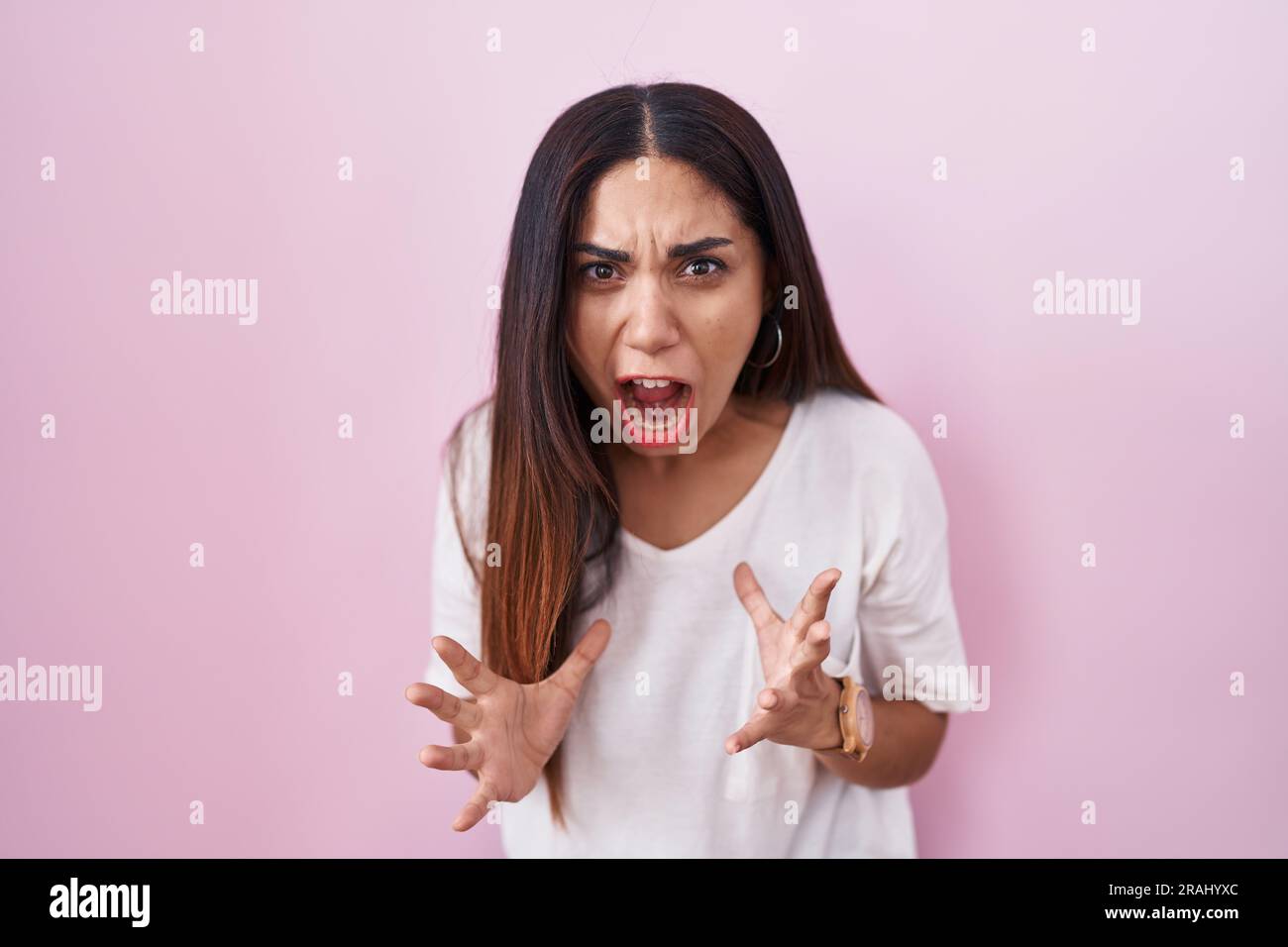 Young arab woman standing over pink background angry and mad screaming ...