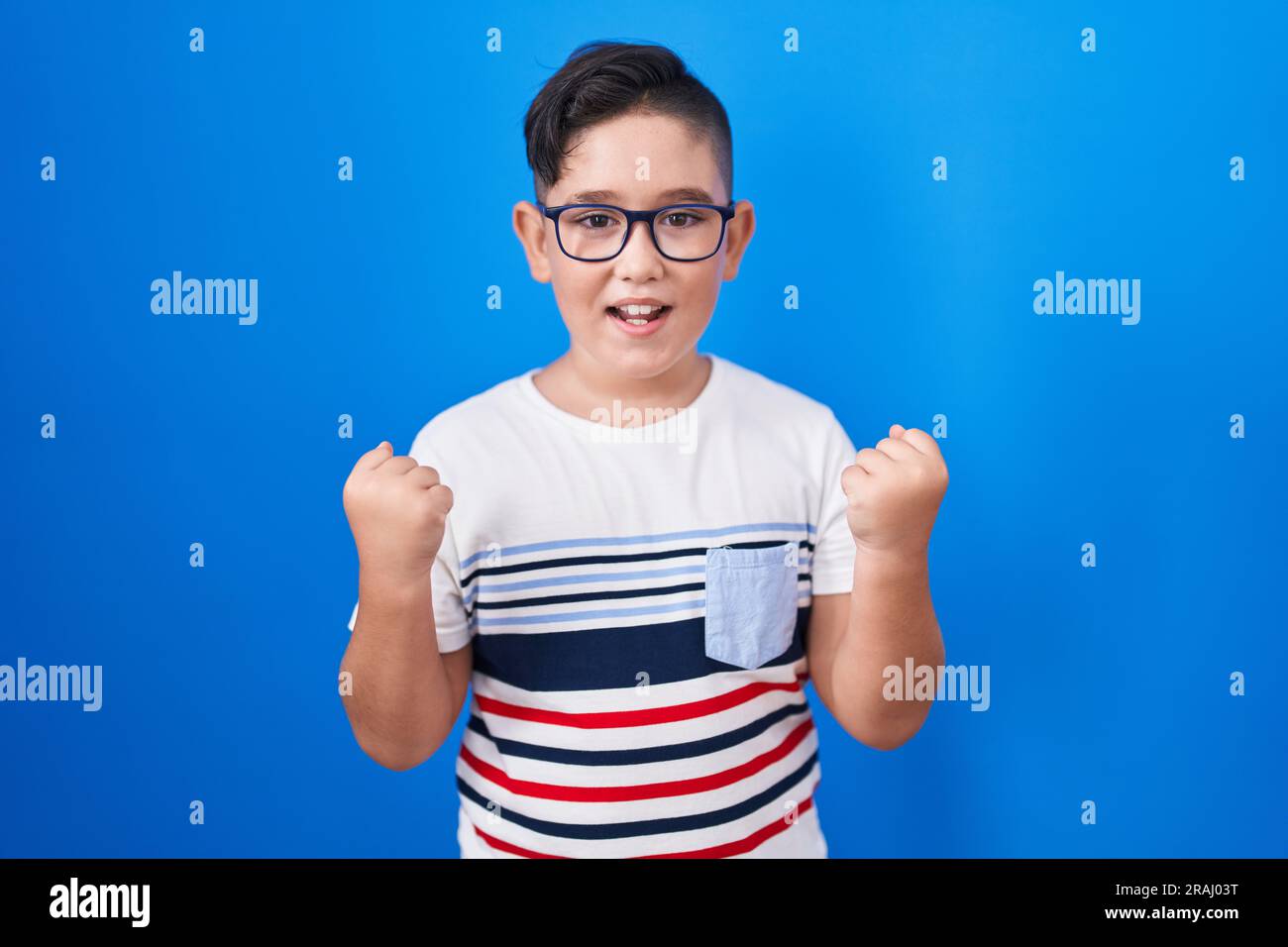 Young hispanic kid standing over blue background celebrating surprised ...
