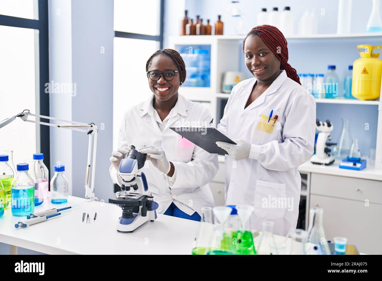 African american women scientists using microscope writing on document at laboratory Stock Photo ...