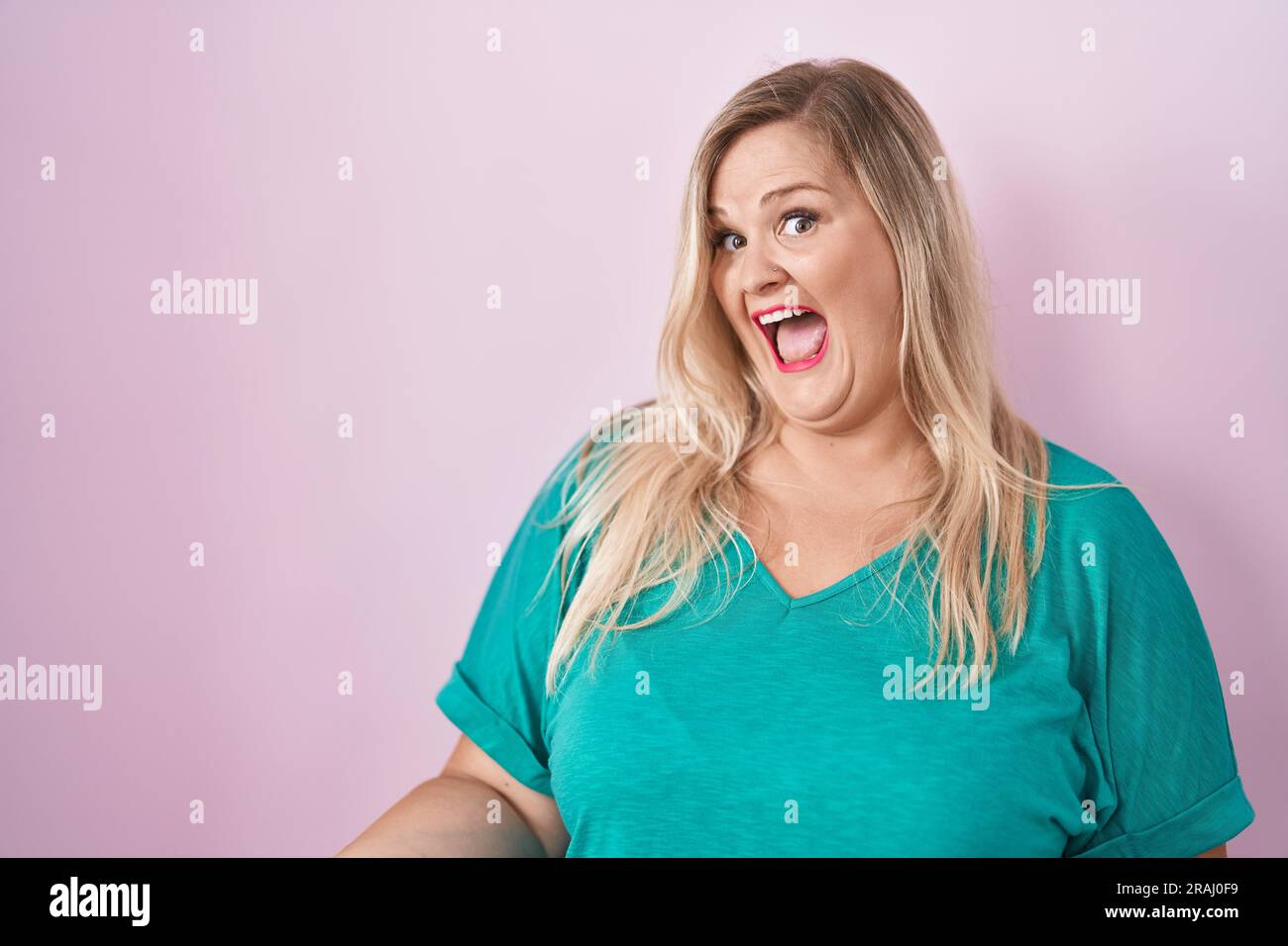 Caucasian plus size woman standing over pink background smiling ...