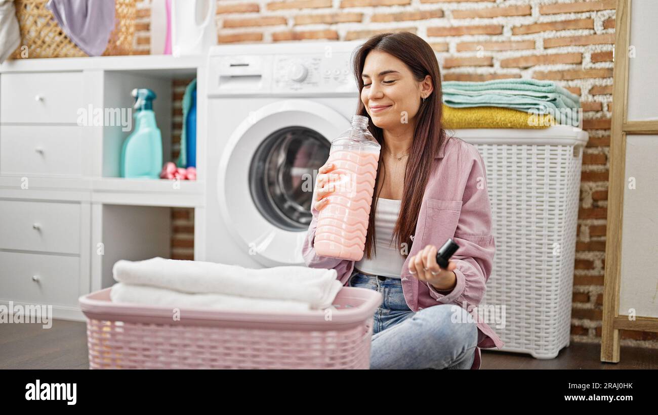 Young beautiful hispanic woman washing clothes smelling detergent ...
