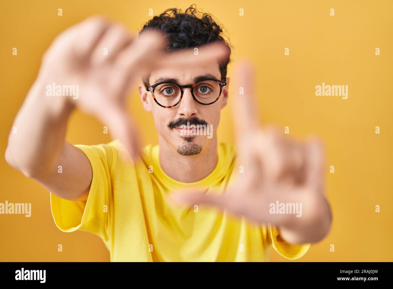 Hispanic man wearing glasses standing over yellow background smiling ...