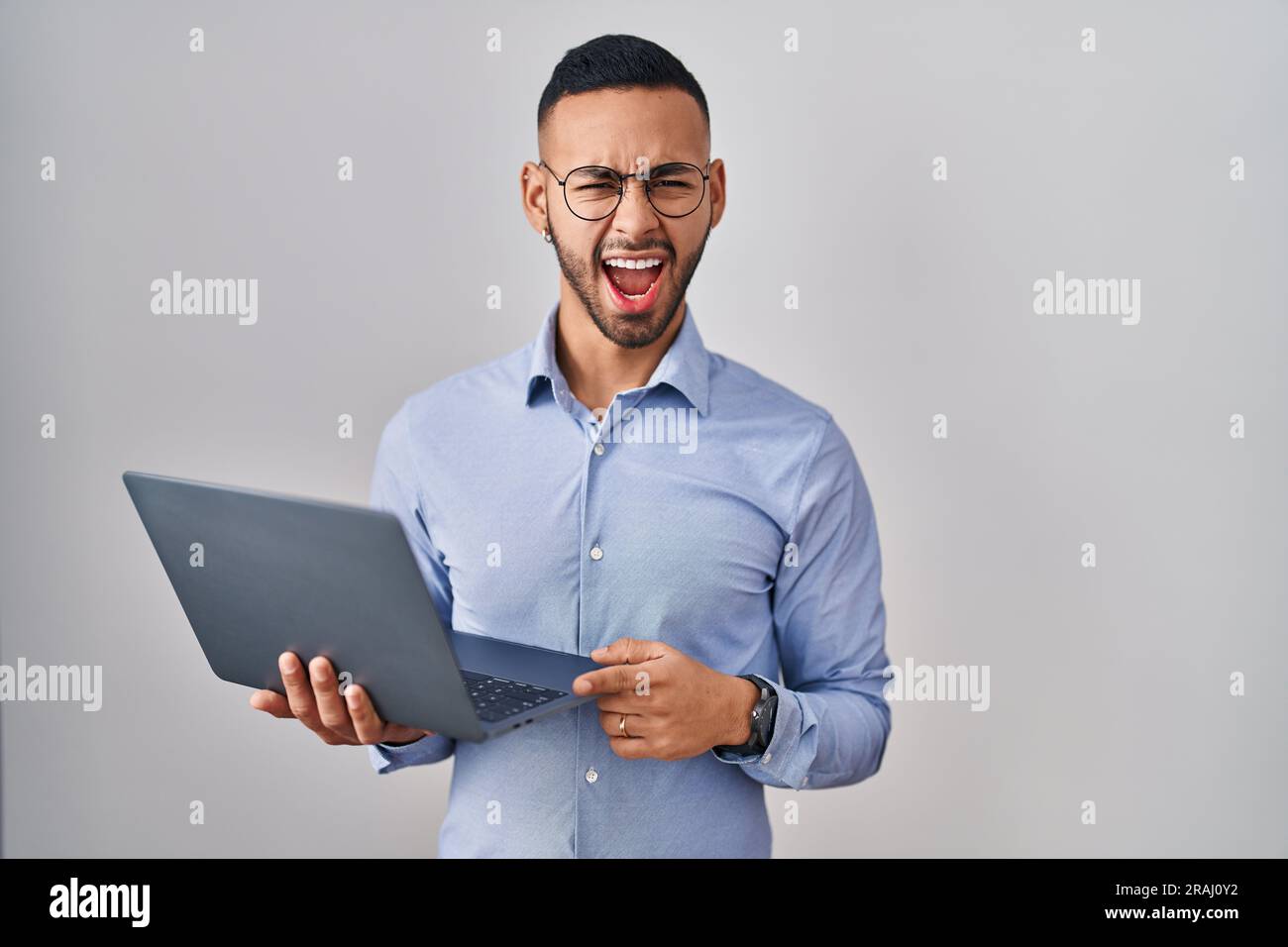 Young hispanic man working using computer laptop angry and mad ...