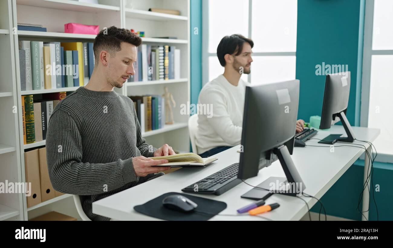 Two men students using computer reading book studying at library ...