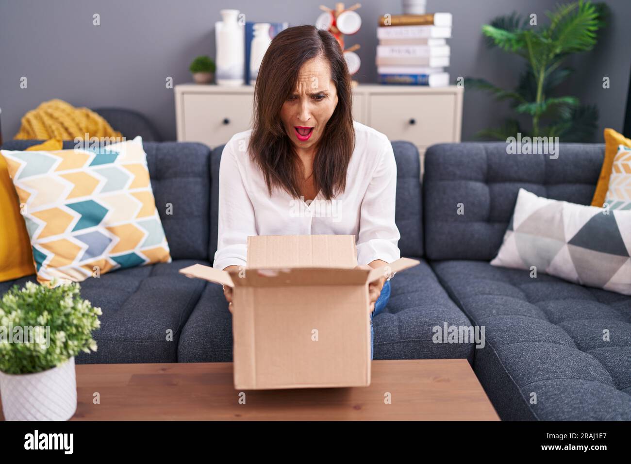 Middle age brunette woman opening cardboard box angry and mad screaming ...