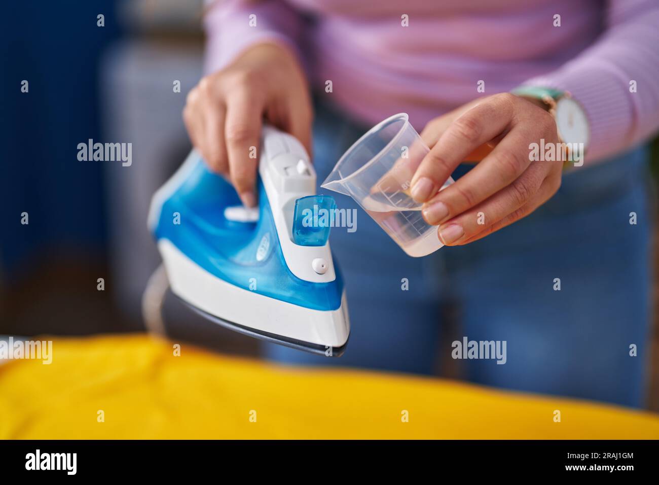 Young hispanic woman pouring water on iron machine at laundry room ...