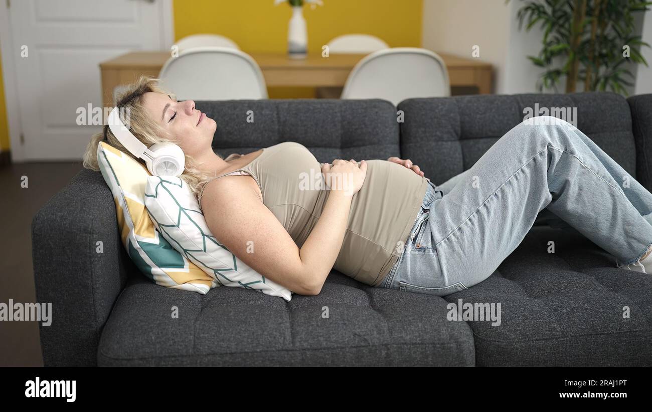 Young pregnant woman listening to music touching belly sleeping on sofa ...