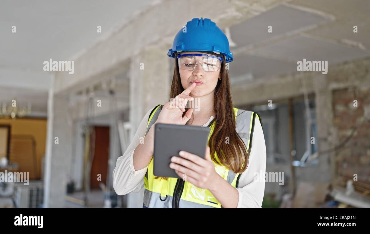 Young beautiful hispanic woman builder using touchpad thinking at ...