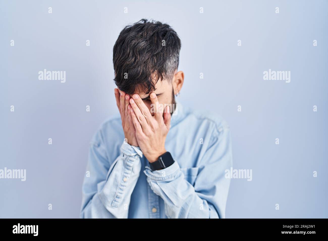 Young hispanic man with beard standing over blue background with sad ...
