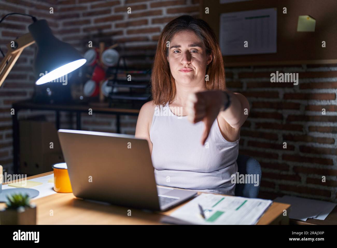 Brunette woman working at the office at night looking unhappy and angry ...