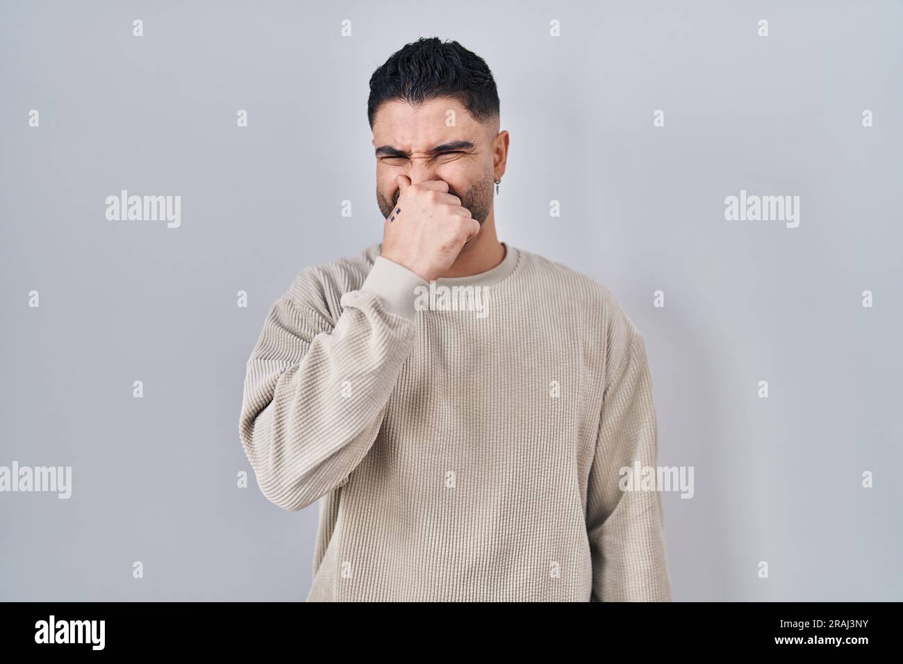 Young handsome man standing over isolated background smelling something ...