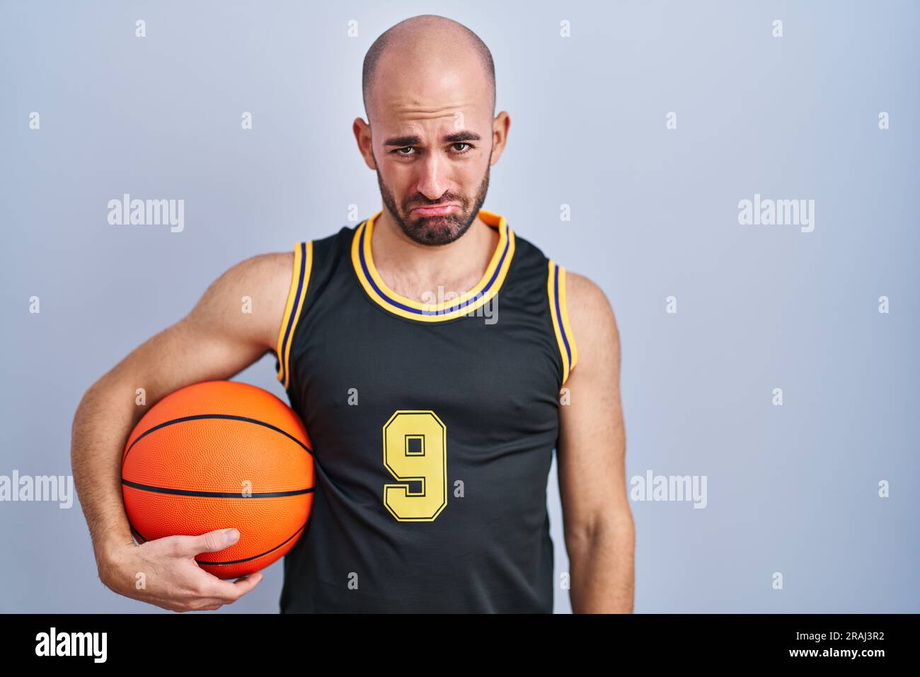 Young bald man with beard wearing basketball uniform holding ball ...