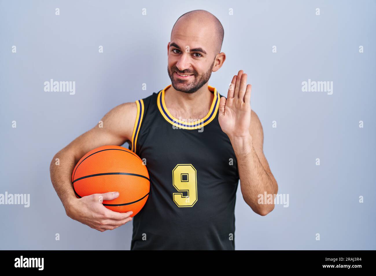 Young bald man with beard wearing basketball uniform holding ball ...