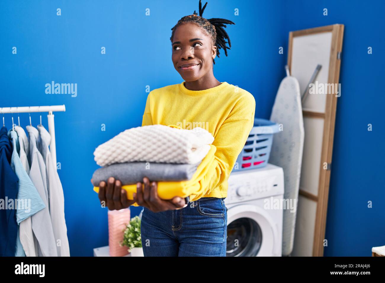 Beautiful black woman holding clean laundry smiling looking to the side ...
