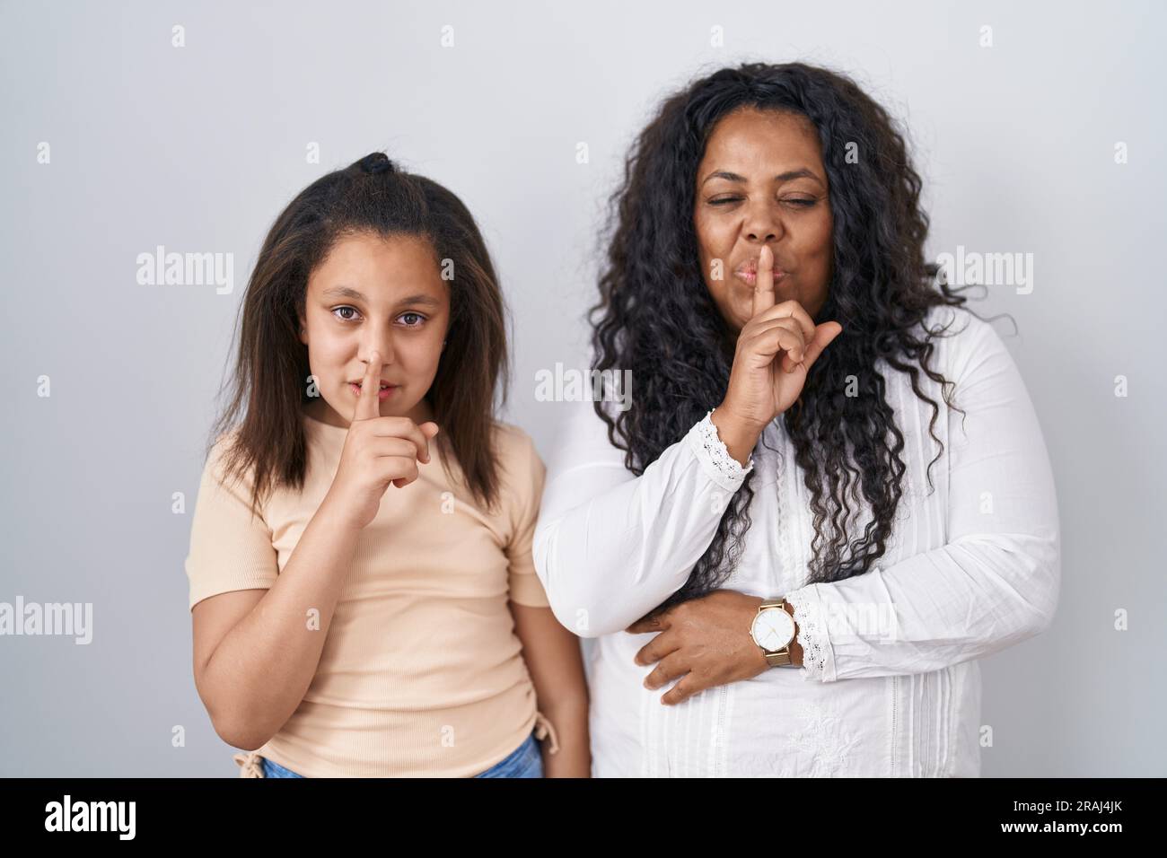 Mother and young daughter standing over white background asking to be ...