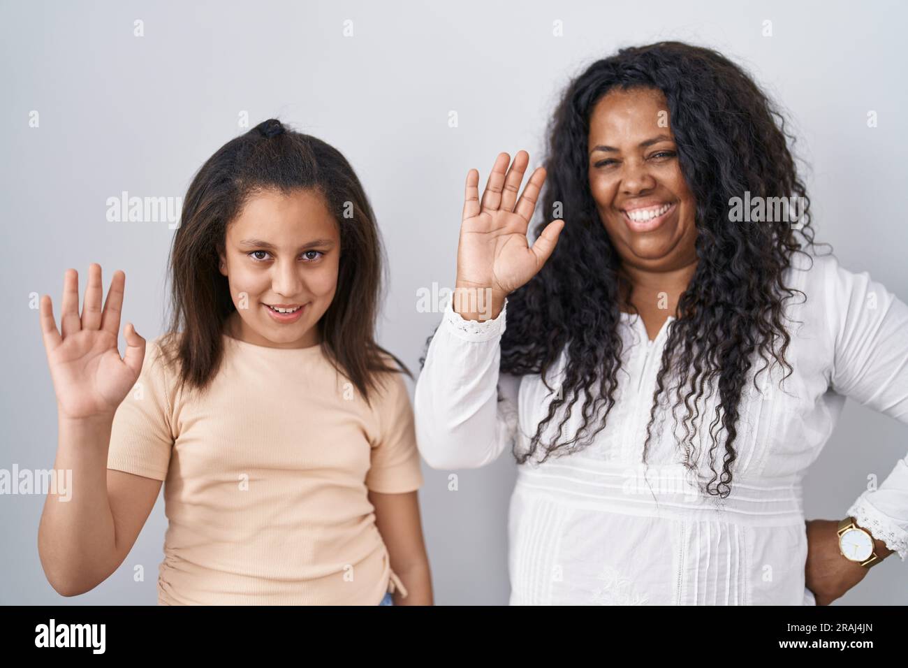 Mother and young daughter standing over white background waiving saying ...