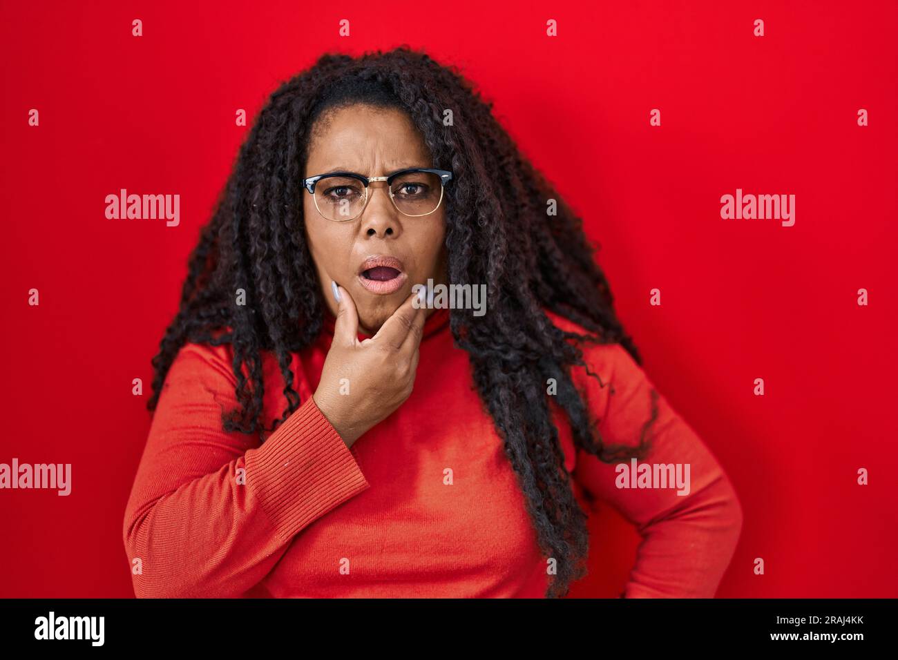 Plus size hispanic woman standing over red background looking ...