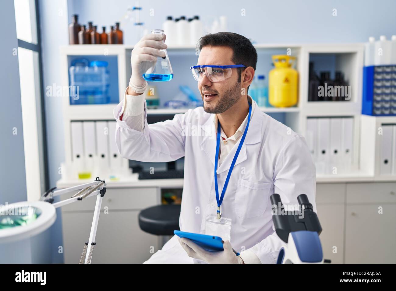 Young hispanic man scientist measuring liquid using touchpad at laboratory Stock Photo - Alamy